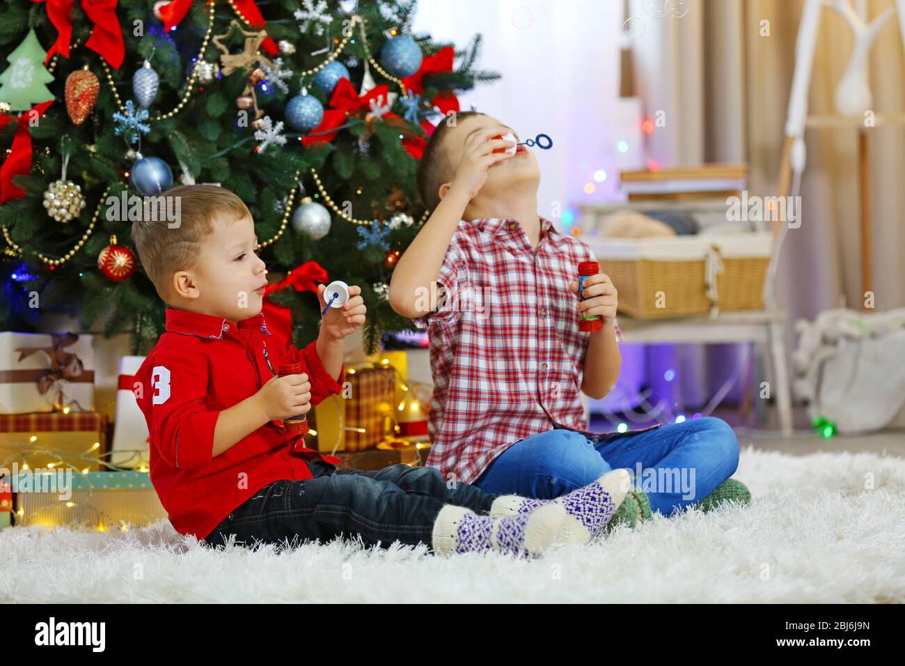 Two cute small brothers blows soap bubbles on Christmas tree background ...