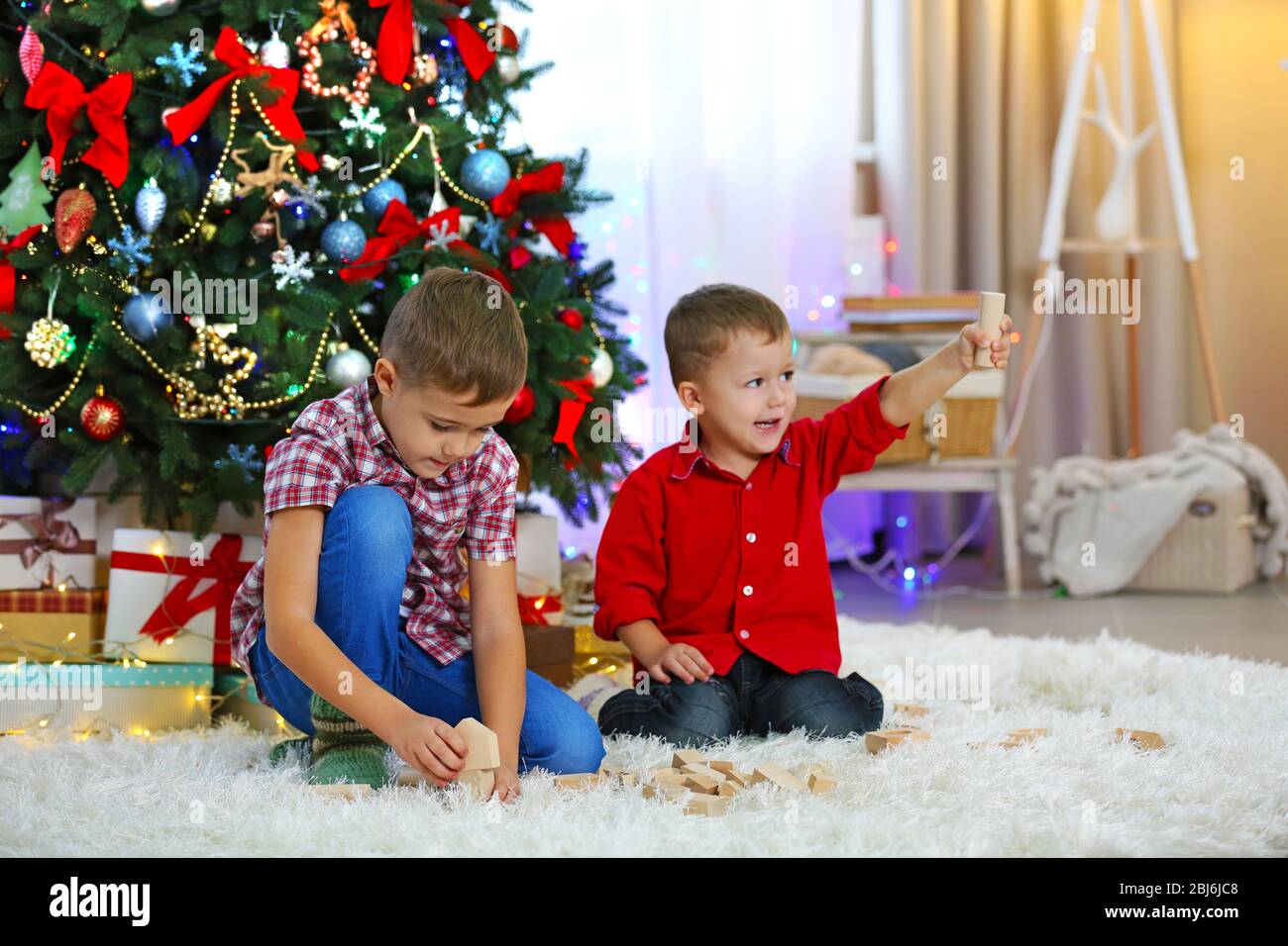 Two cute small brothers playing with wooden toys on Christmas tree ...