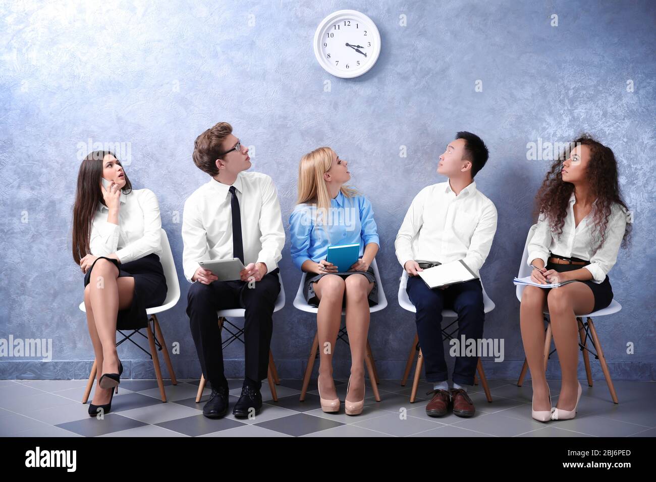 Young people sitting on a chairs in grey hall Stock Photo - Alamy