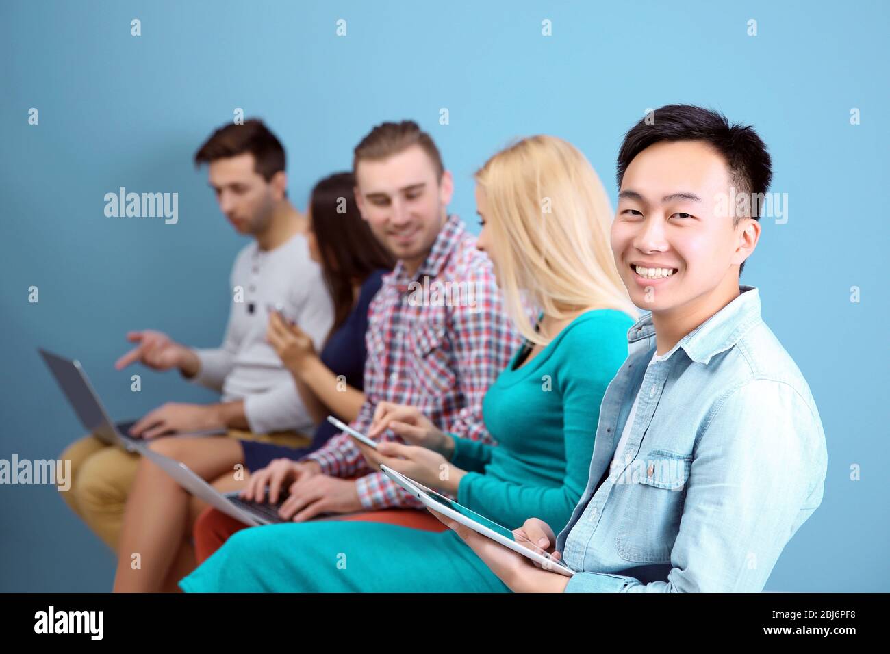 Young people sitting on a chairs and using devices in blue hall, close ...