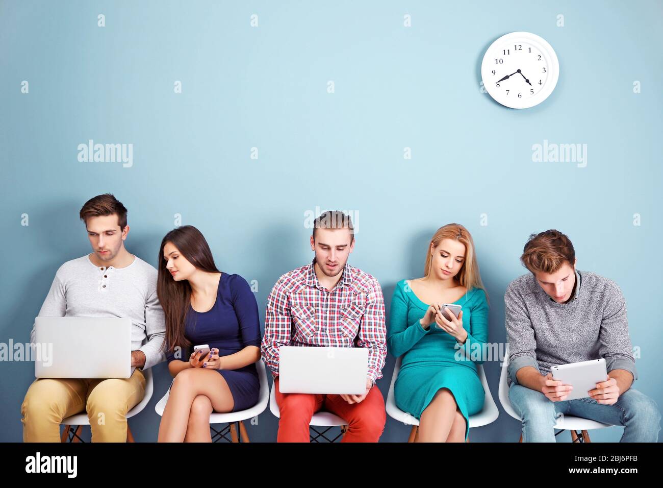 Young people sitting on a chairs and using devices in blue hall Stock ...