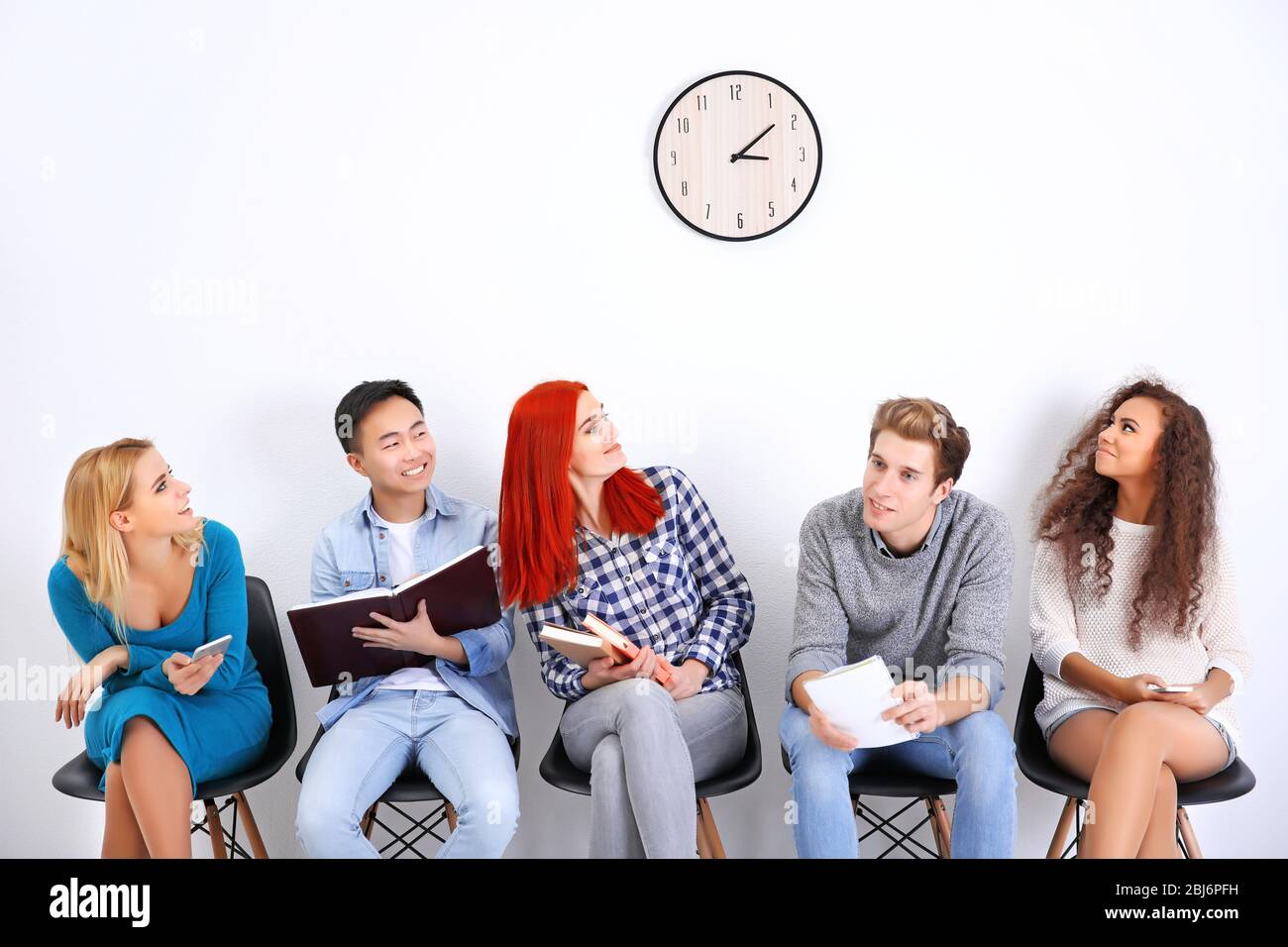 Young people sitting on a chairs in white hall Stock Photo - Alamy