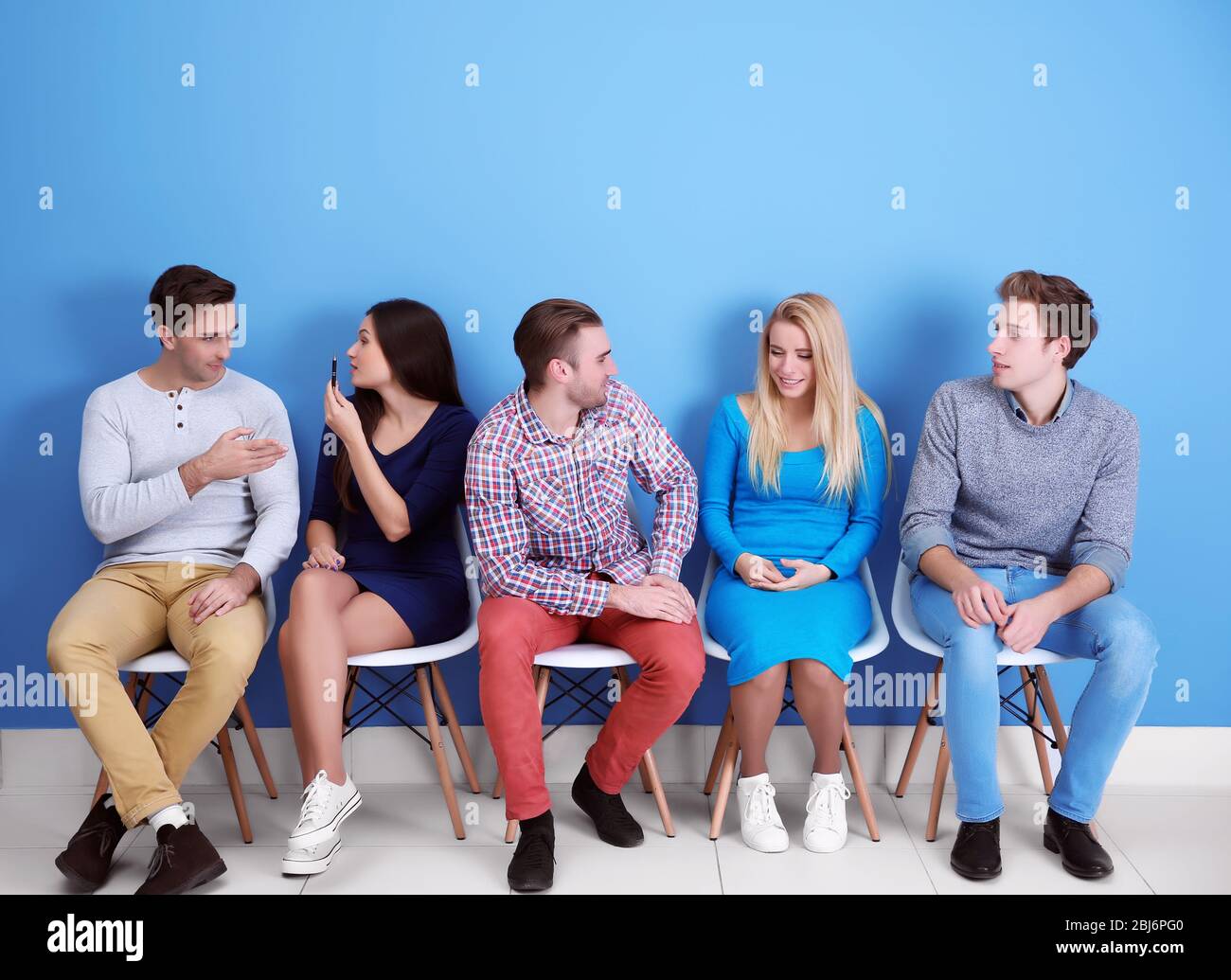 Young people sitting on a chairs near in blue hall Stock Photo - Alamy