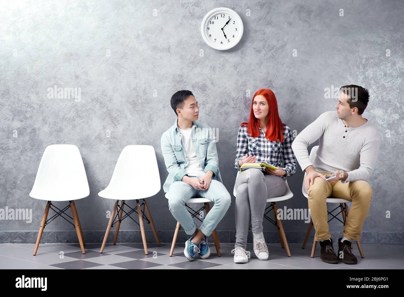 Young people sitting on a chairs in grey hall Stock Photo - Alamy