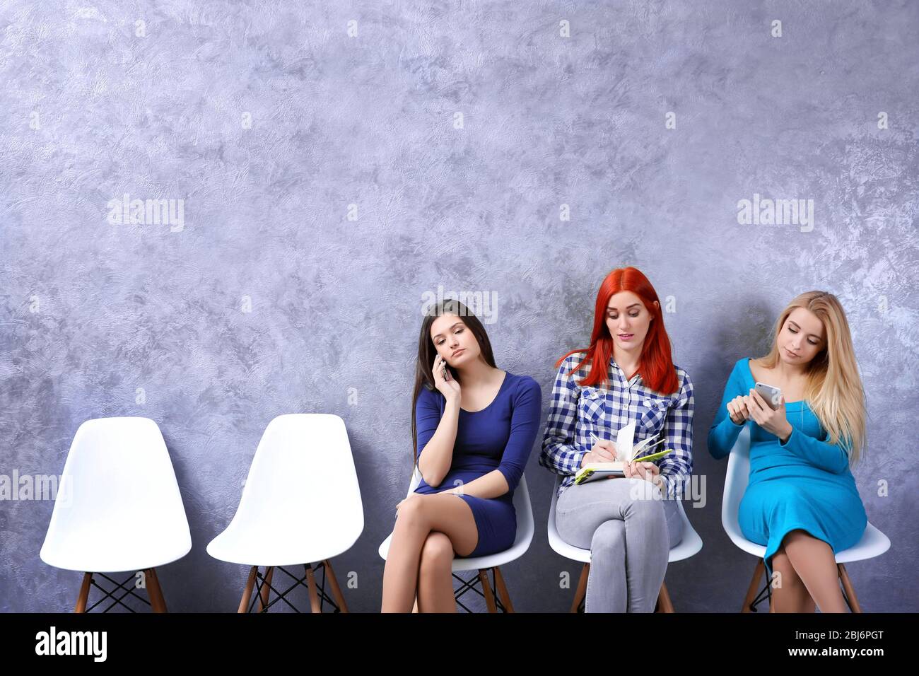 Young girls sitting on a chairs in grey hall Stock Photo - Alamy