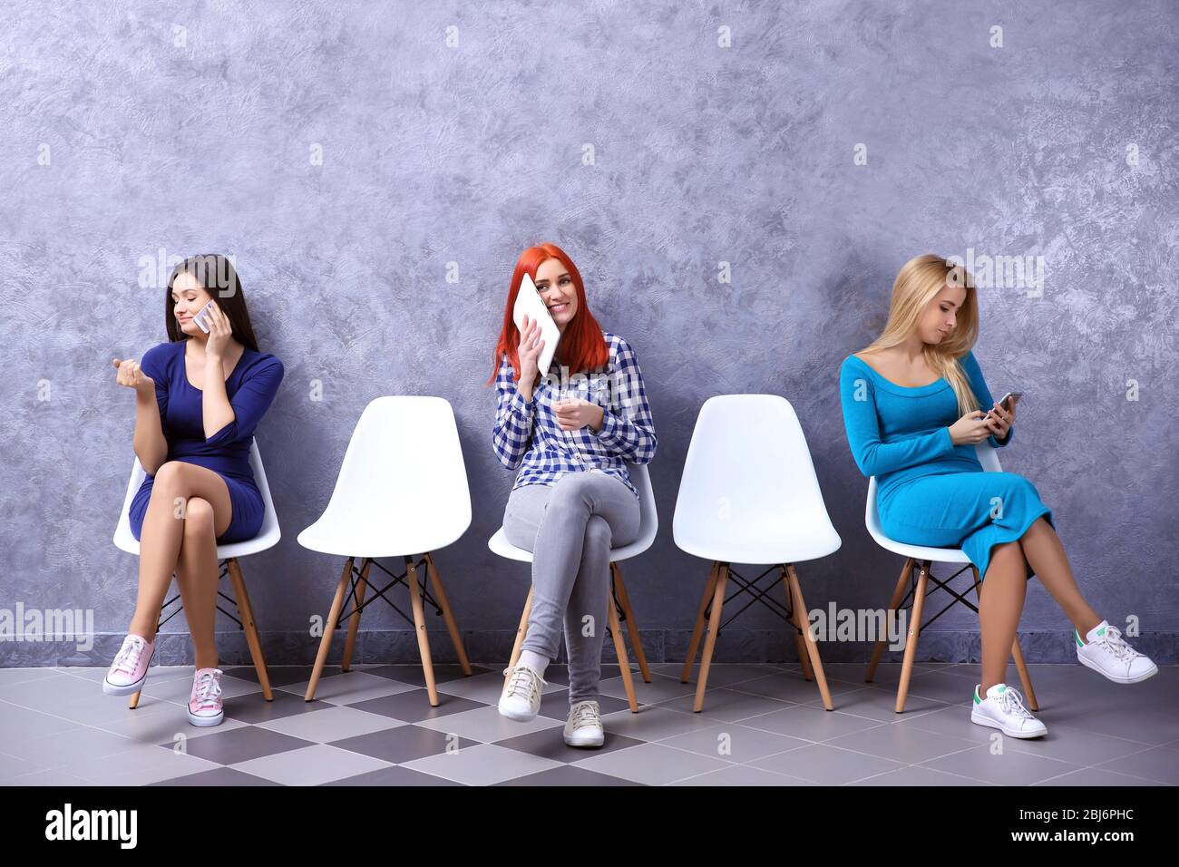 Young girls sitting on a chairs in grey hall Stock Photo - Alamy