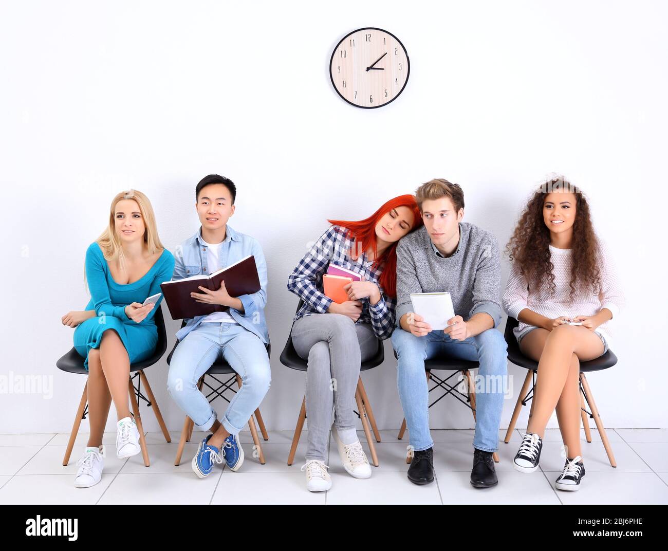 Young people sitting on a chairs in white hall Stock Photo - Alamy