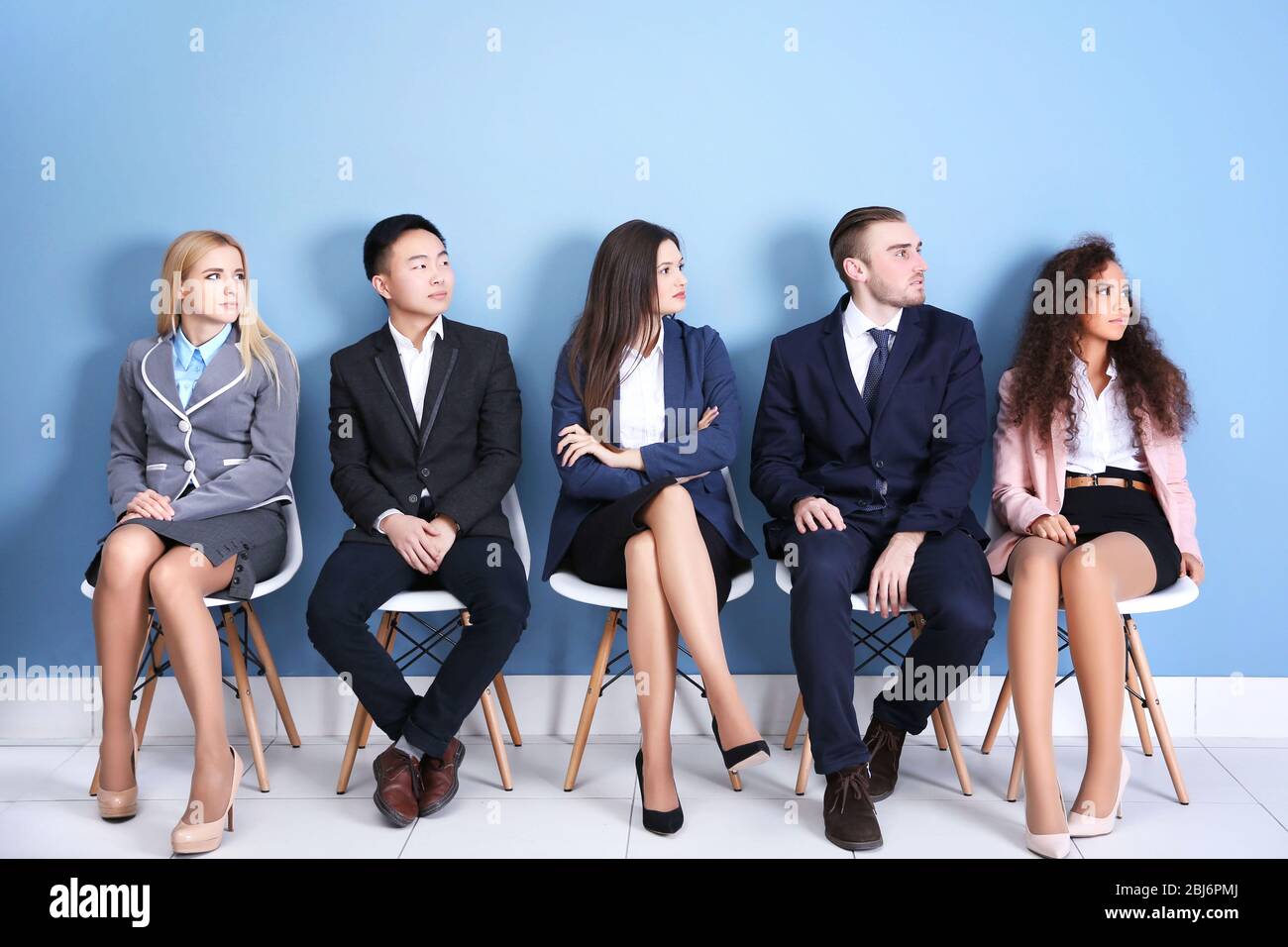 Young people sitting and looking left on a chairs in blue hall Stock ...