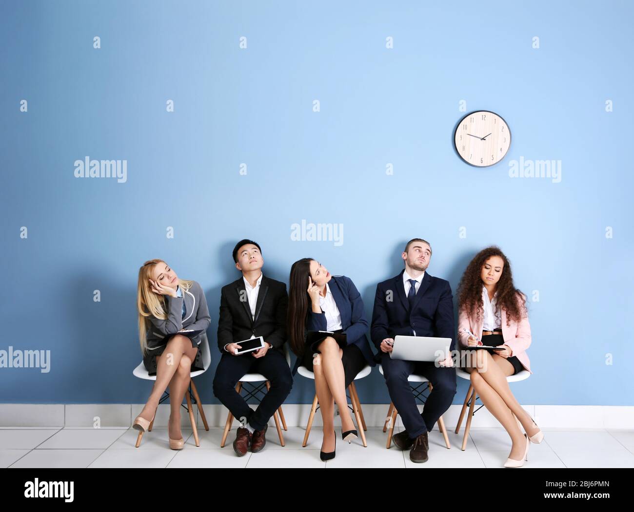 Young people sitting on a chairs and looking at the clock in blue hall ...