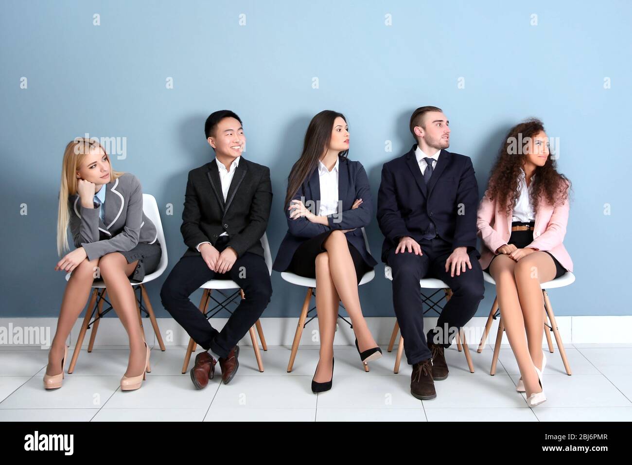 Young people sitting and looking left on a chairs in blue hall Stock ...