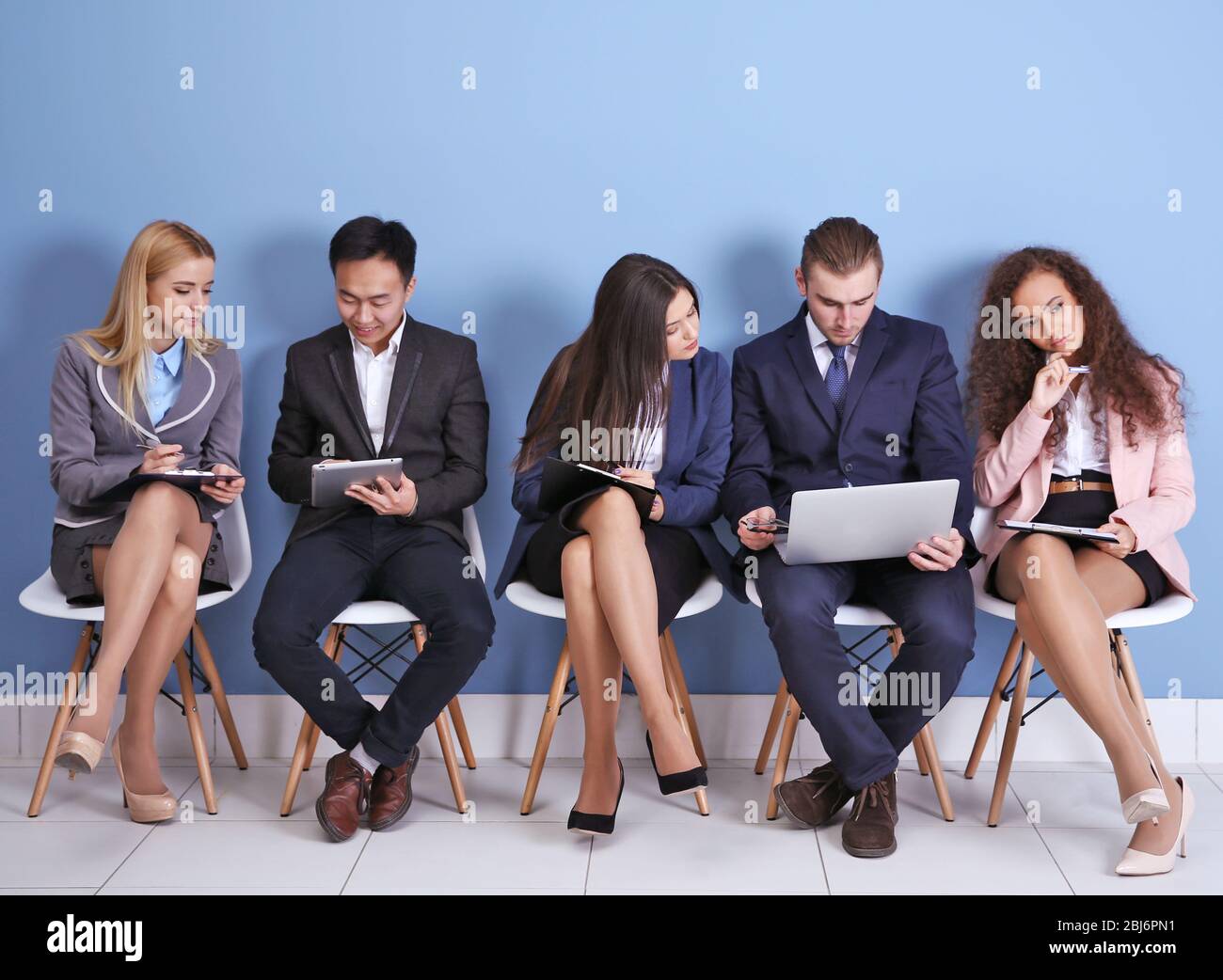 Young people sitting on a chairs, making notes and using devices in ...