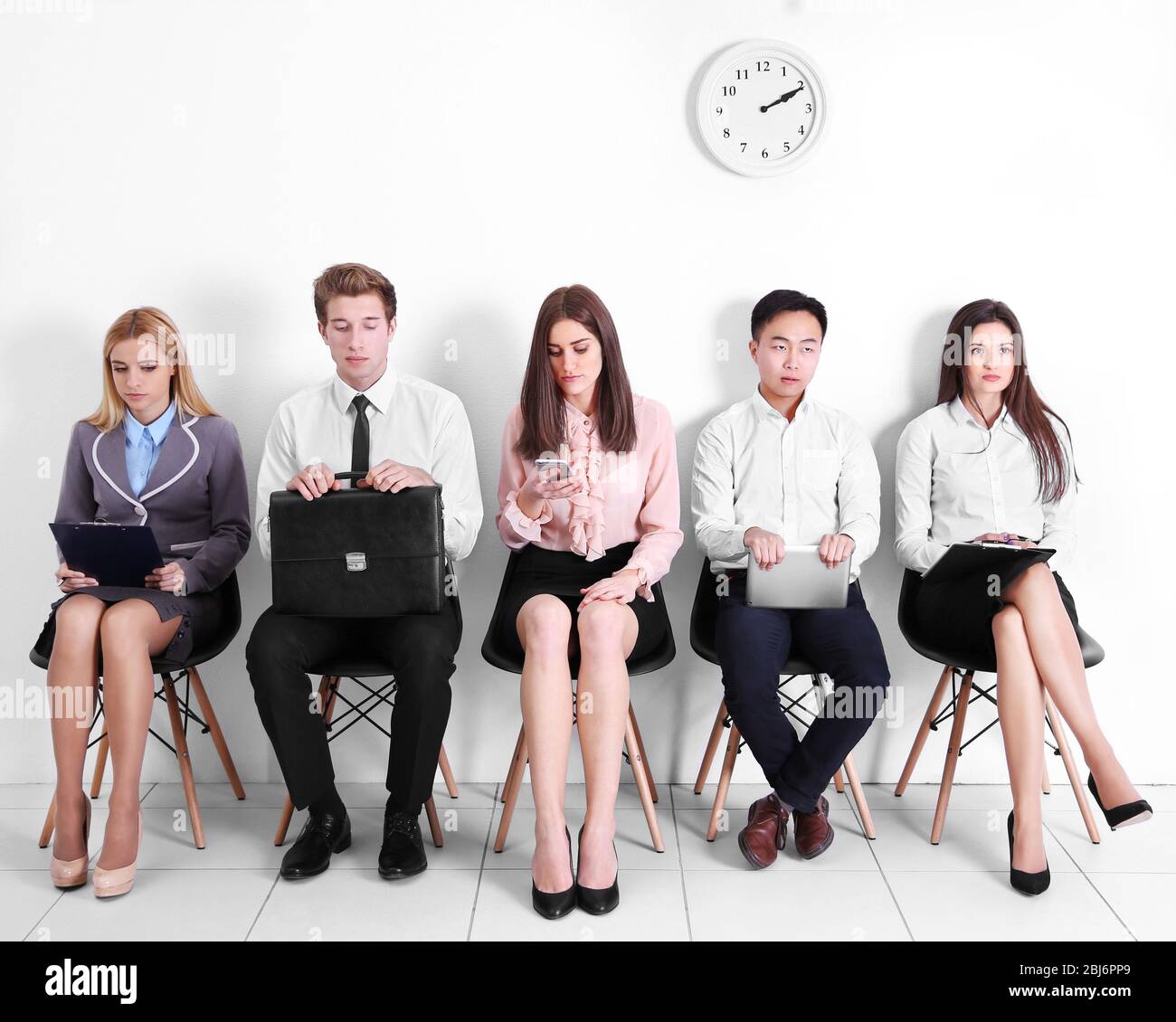 Young people sitting on a chairs in white hall Stock Photo - Alamy