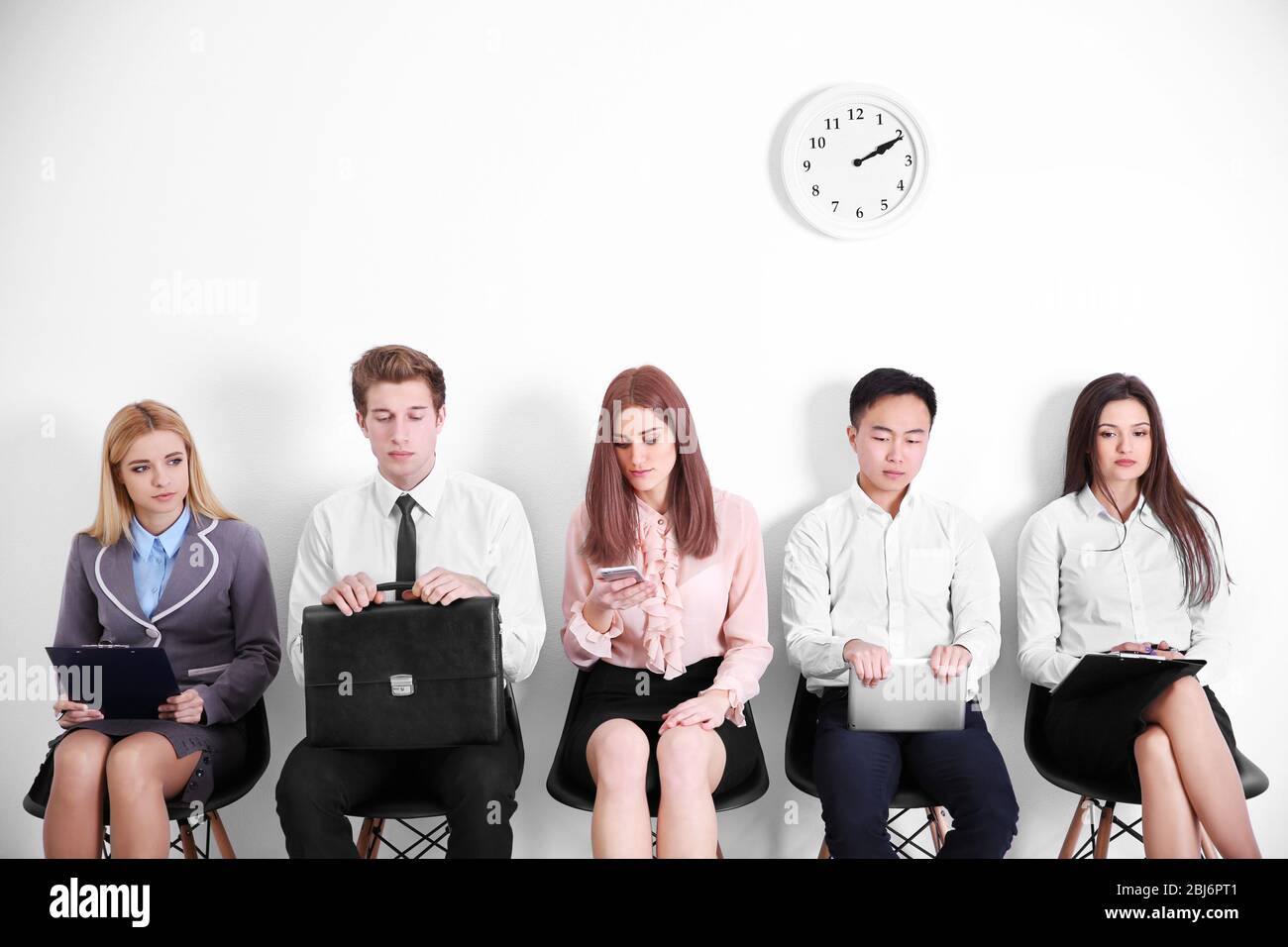 Young people sitting on a chairs in white hall Stock Photo - Alamy