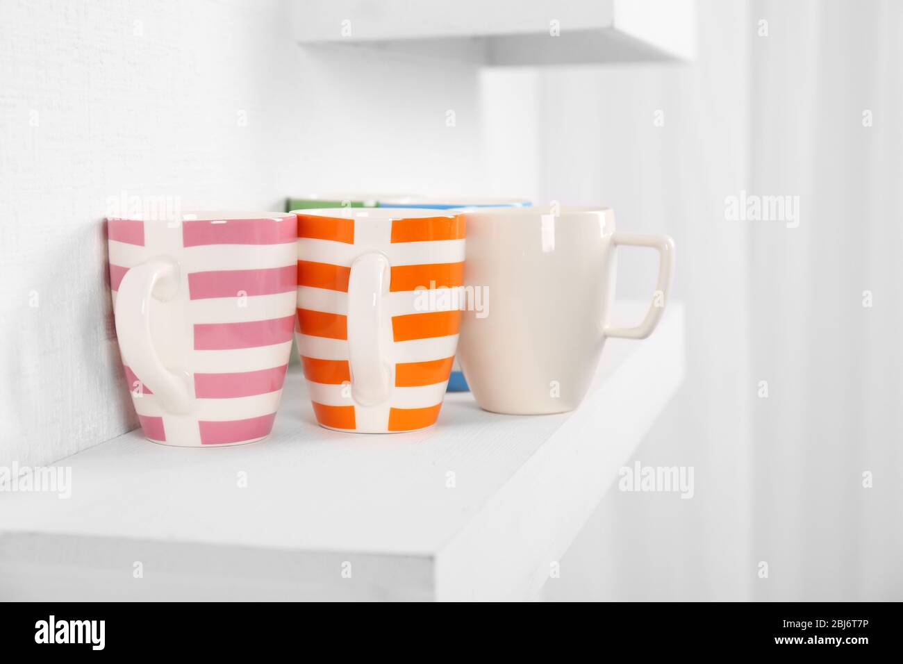 Set of striped cups on shelf against white wall background Stock Photo ...