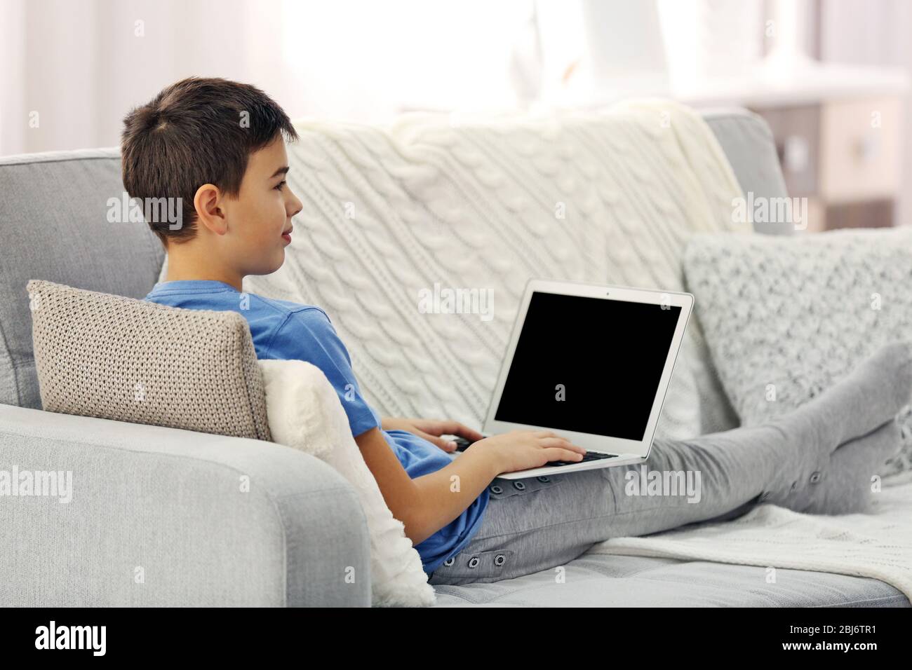 Boy with laptop sitting on a sofa Stock Photo - Alamy