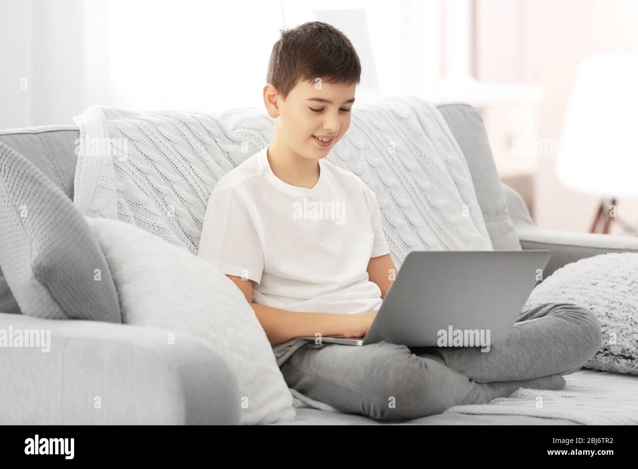 Boy using laptop on a sofa at home Stock Photo - Alamy