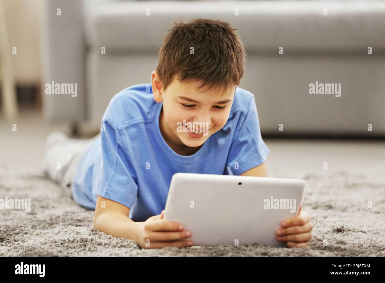 Boy reading tablet on a carpet at home Stock Photo - Alamy
