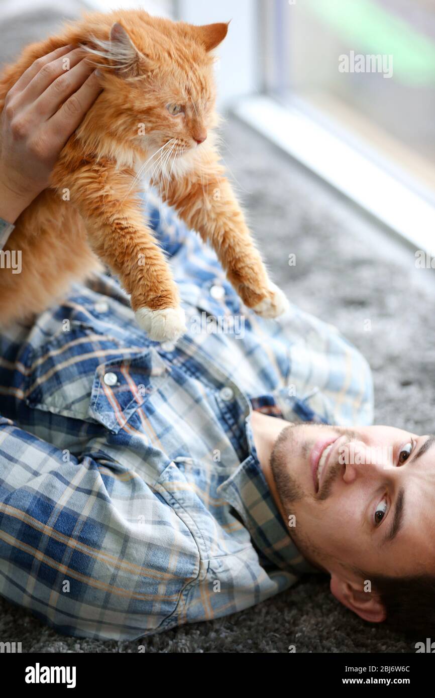 Young man with fluffy cat lying on a carpet Stock Photo - Alamy