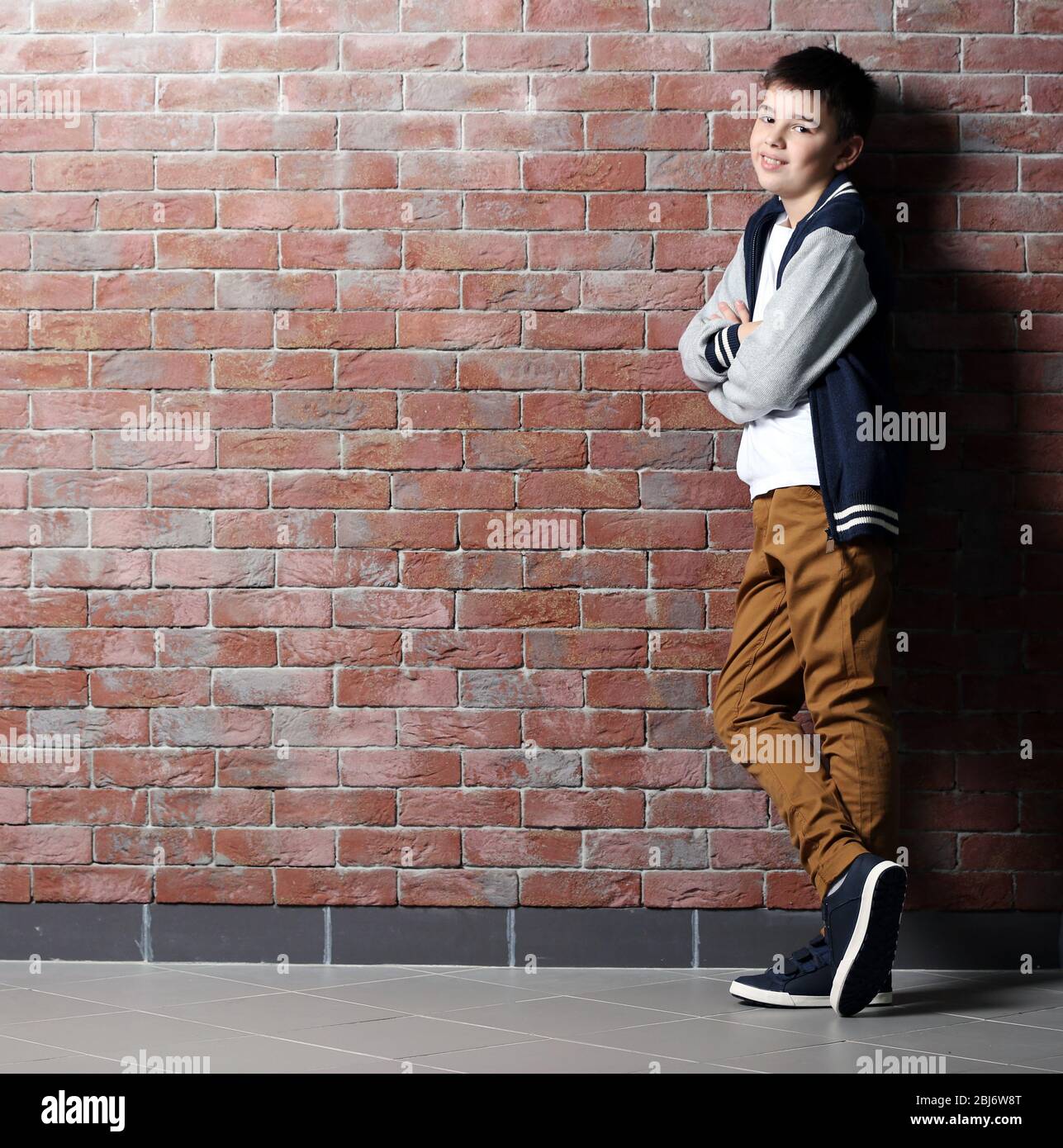 Cute little boy standing near brick wall Stock Photo - Alamy