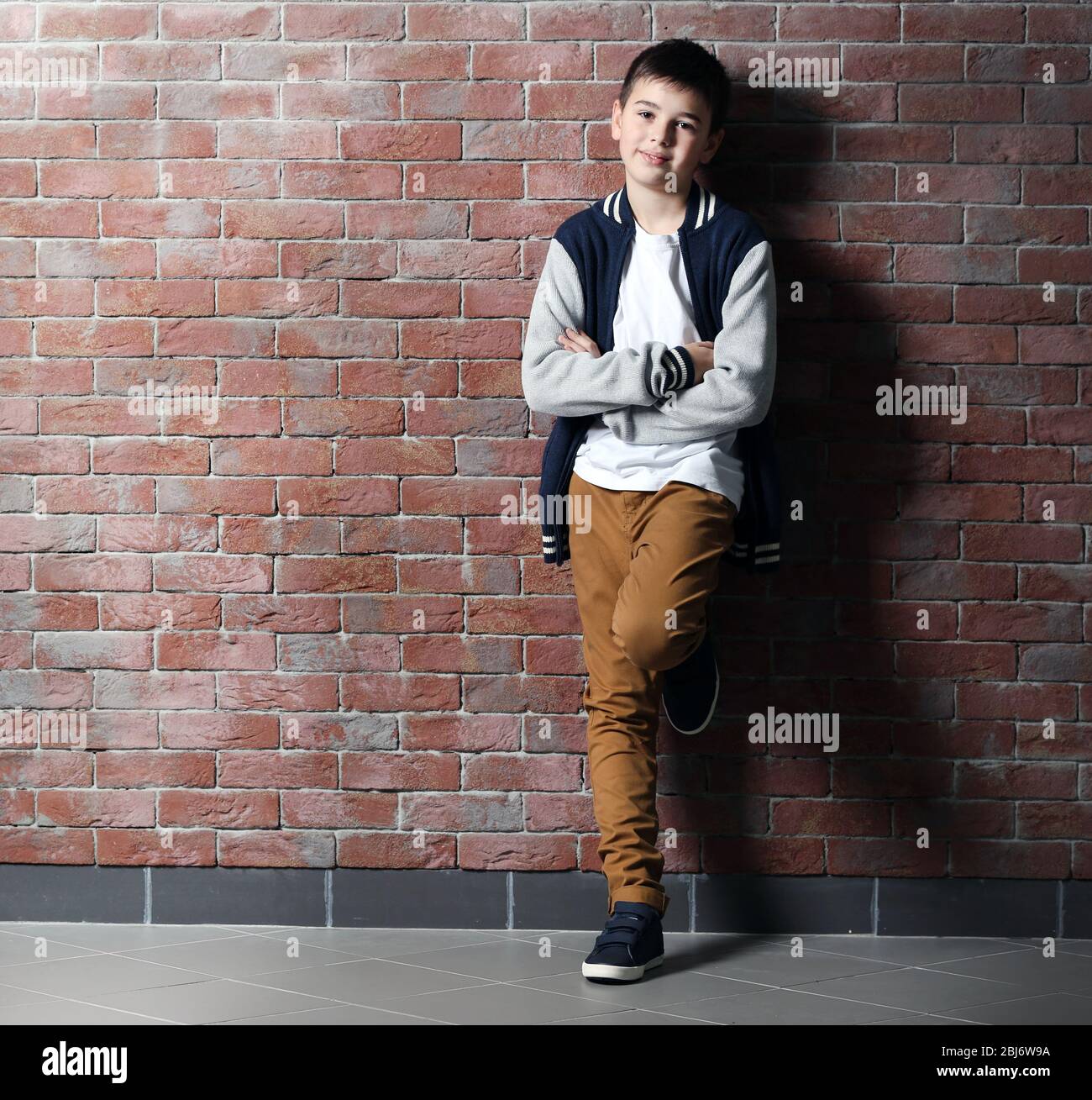 Cute little boy standing near brick wall Stock Photo - Alamy