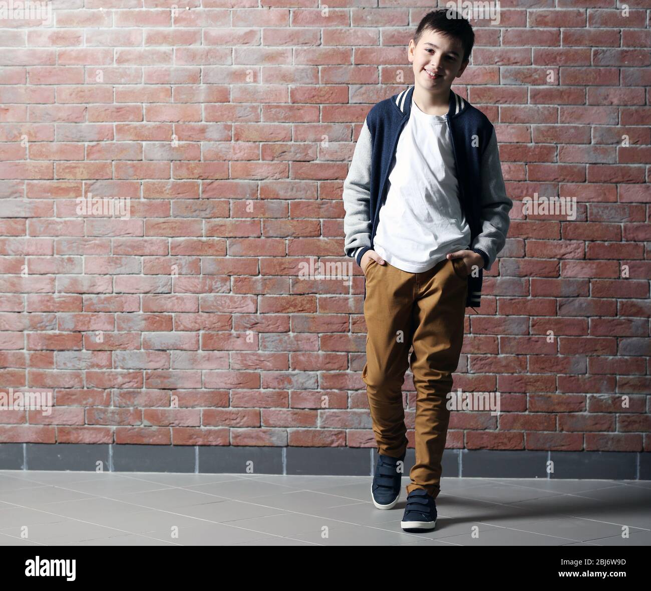 Cute little boy standing near brick wall Stock Photo - Alamy