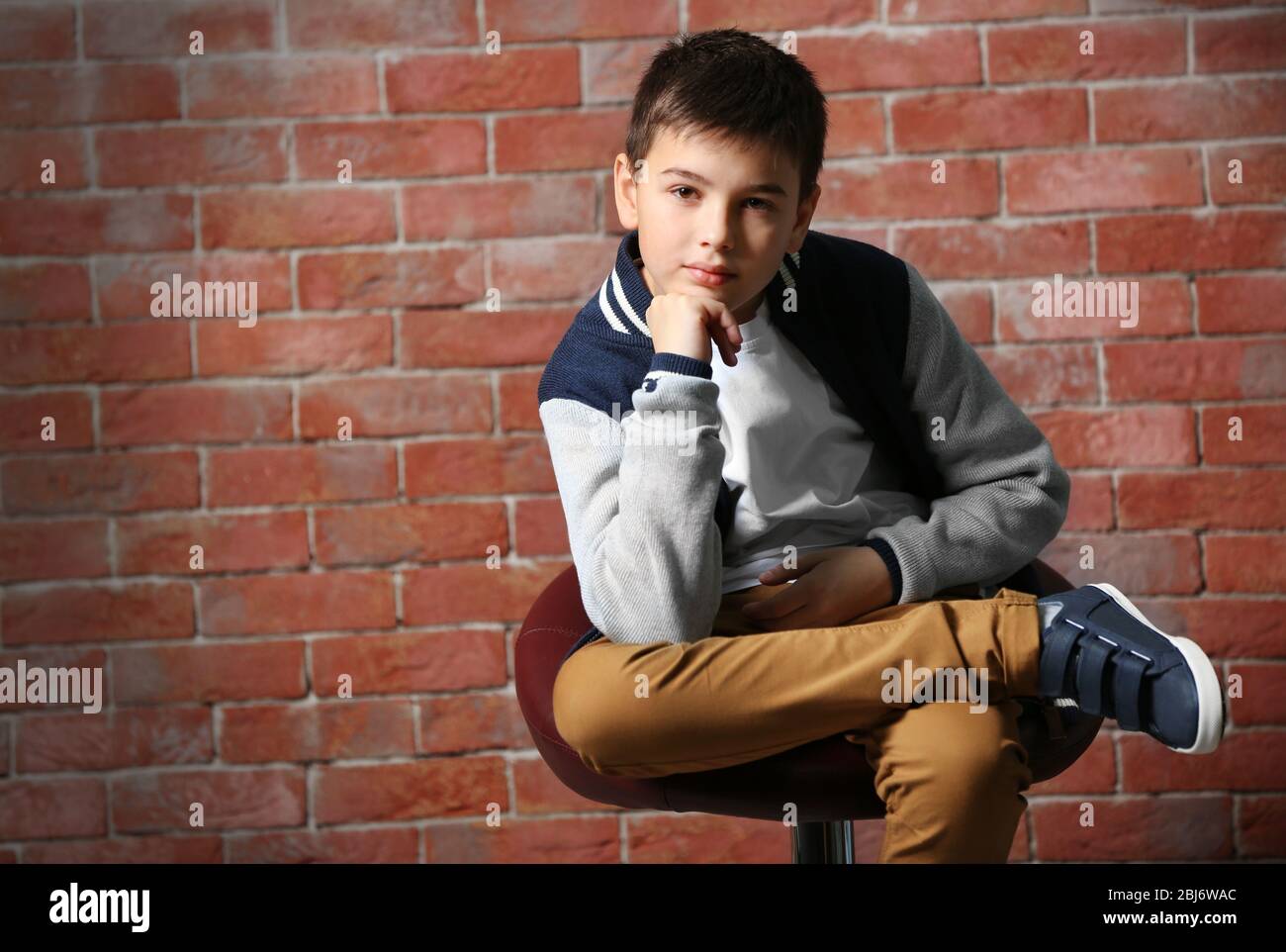 Cute little boy sitting on a chair near brick wall Stock Photo - Alamy