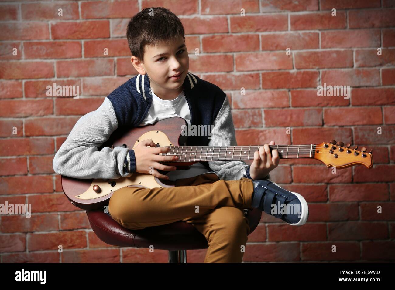 Cute little boy playing guitar on brick wall background Stock Photo - Alamy