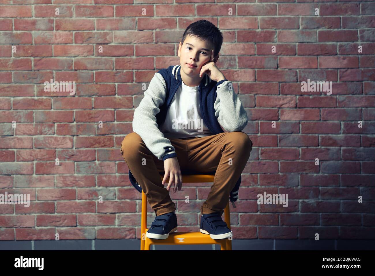 Cute little boy sitting on a chair near brick wall Stock Photo - Alamy