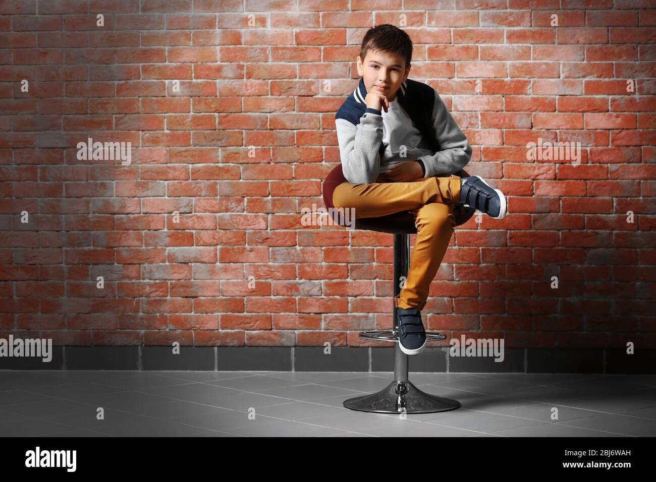 Cute little boy sitting on a chair near brick wall Stock Photo - Alamy