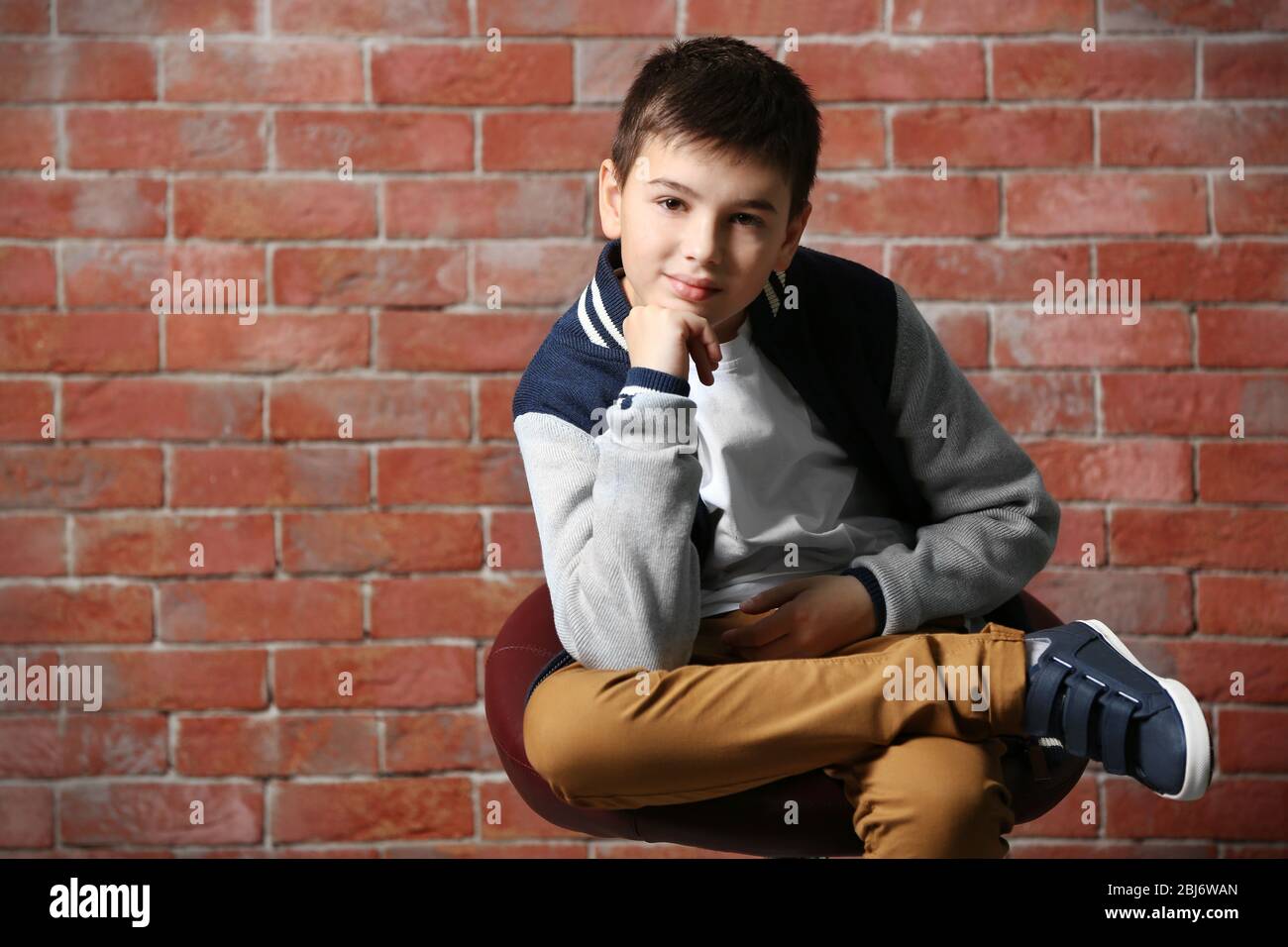 Cute little boy sitting on a chair near brick wall Stock Photo - Alamy