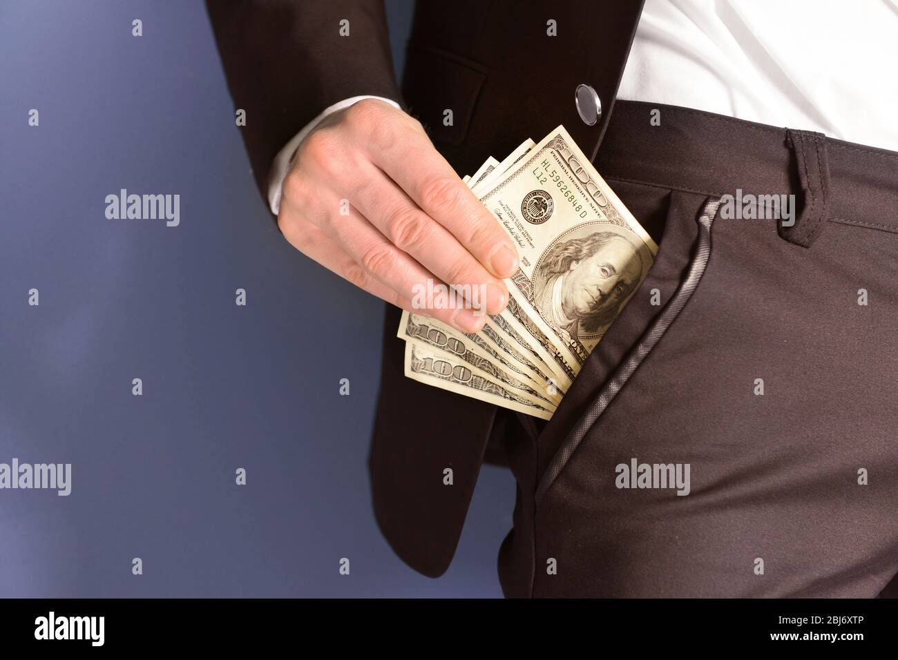 Man getting dollar banknotes out of suit pocket on grey background ...