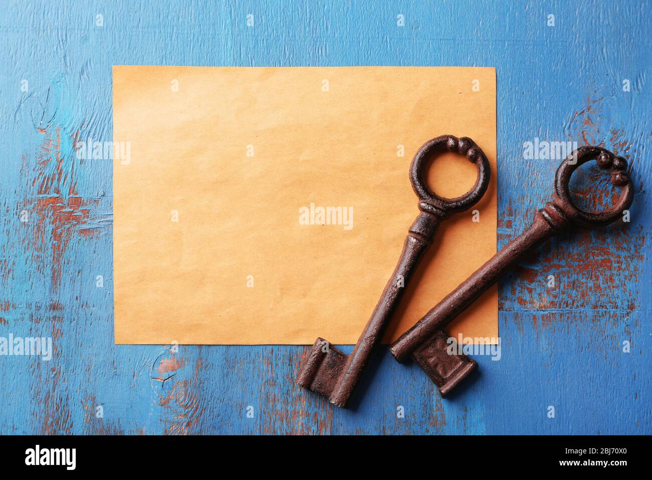 Old key with empty sheet of paper on blue wooden background, close up ...