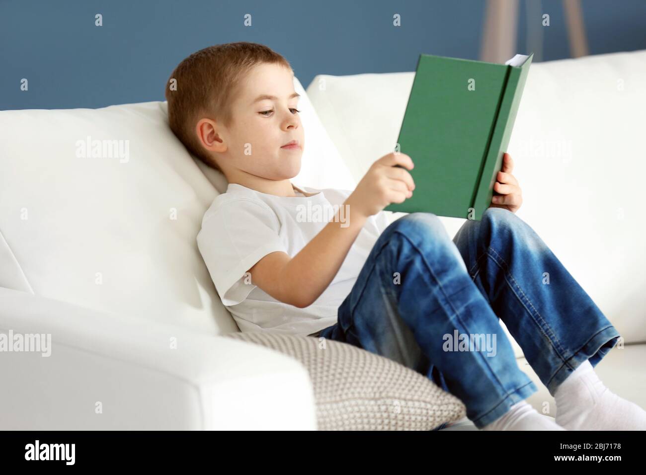 Little boy reading book on a sofa at home Stock Photo - Alamy