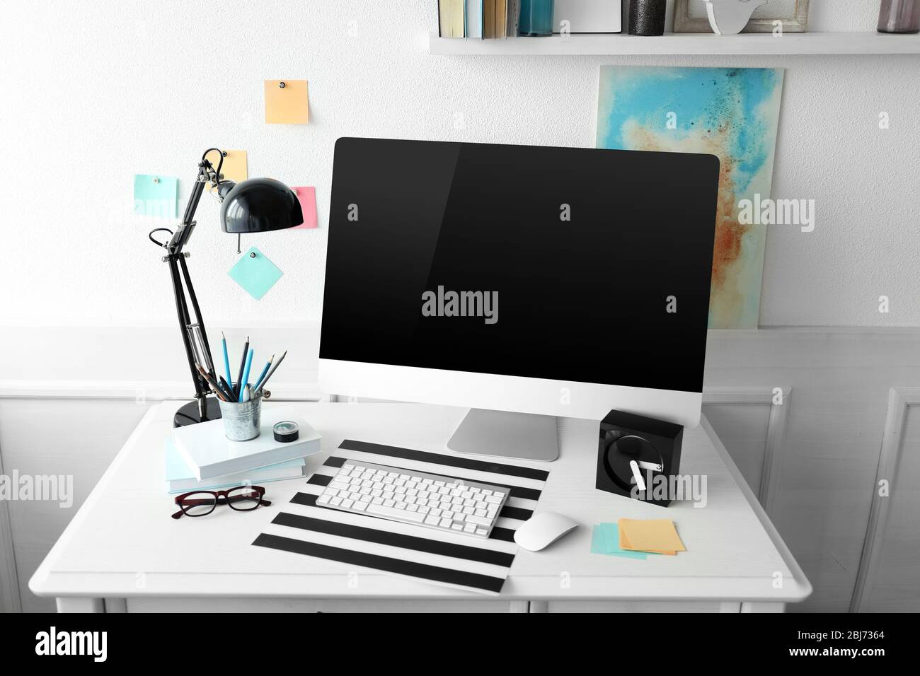 Modern wide screen monitor and lamp on white table in room interior ...