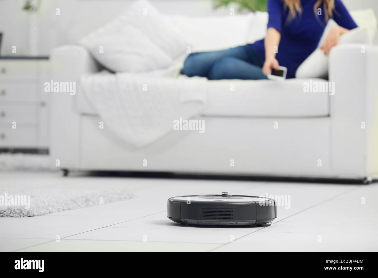 Robotic vacuum cleaner cleaning the room while woman resting on sofa ...