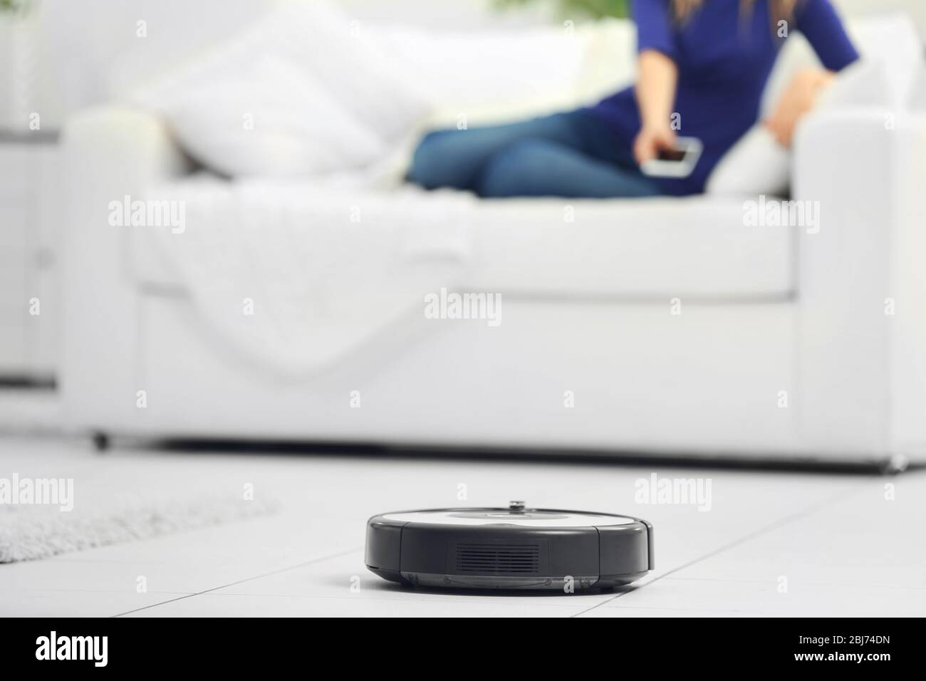 Robotic vacuum cleaner cleaning the room while woman resting on sofa ...