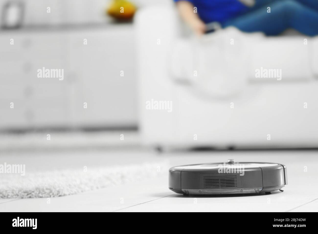 Robotic vacuum cleaner cleaning the room while woman resting on sofa ...