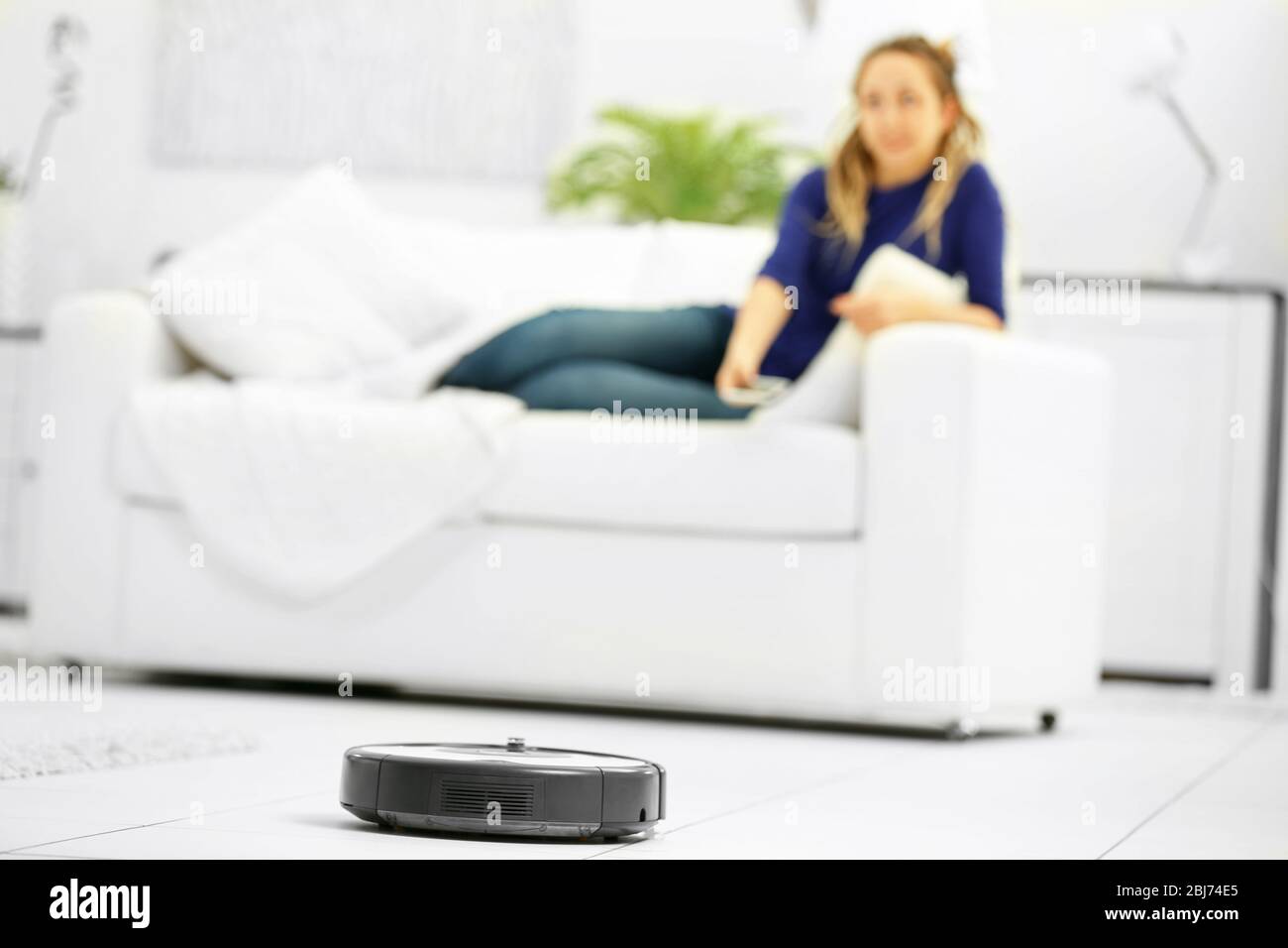 Robotic vacuum cleaner cleaning the room while woman resting on sofa ...