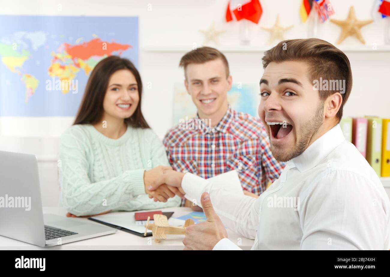 Happy agent and young couple handshaking in the office of travel ...