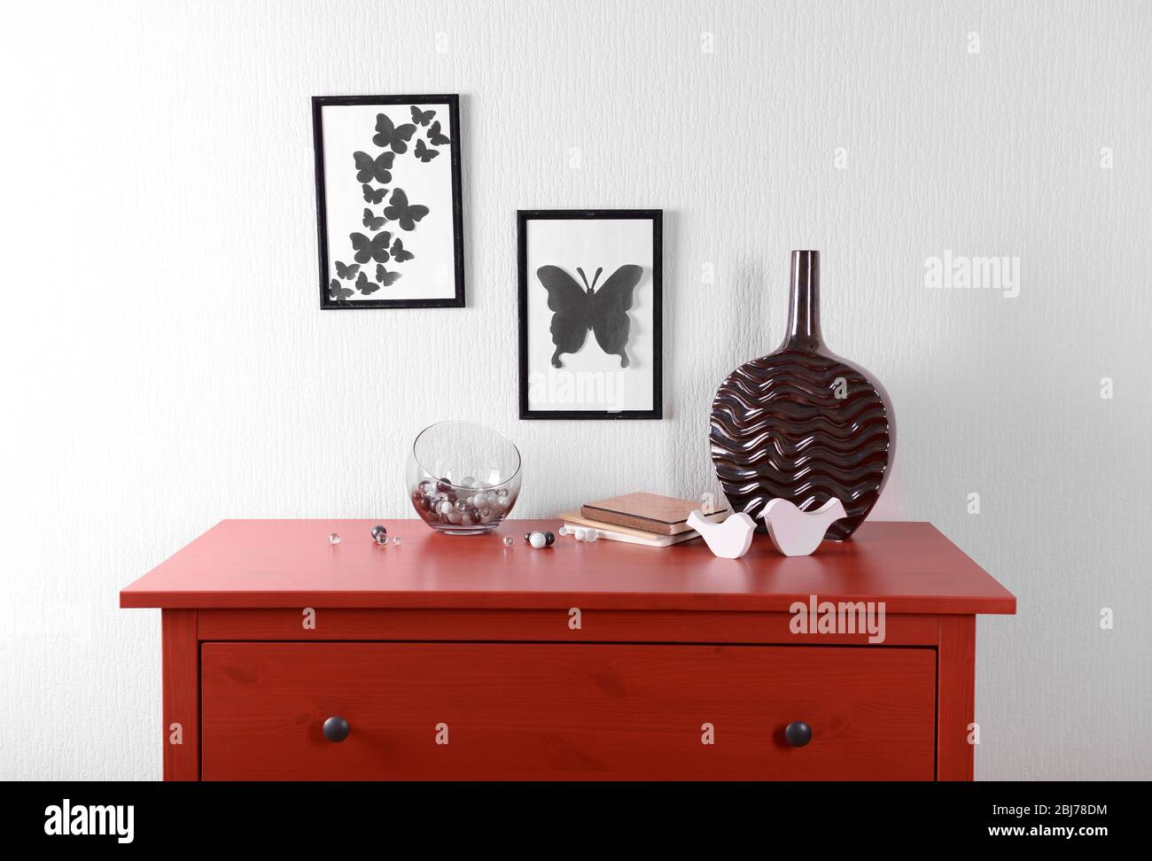 Room interior with red wooden commode, vase and frames on light wall ...
