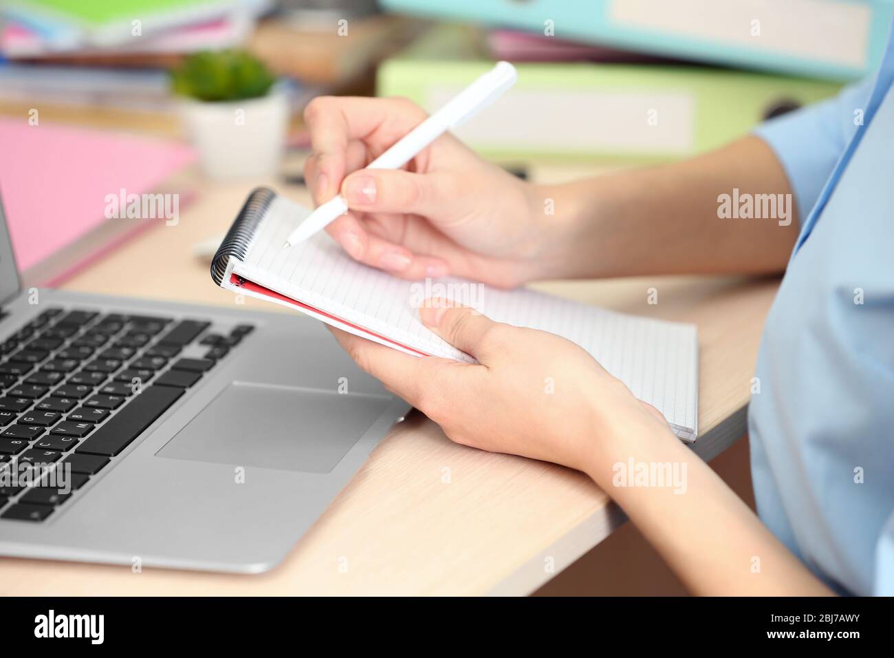 Woman making notes in a notebook with laptop beside Stock Photo - Alamy