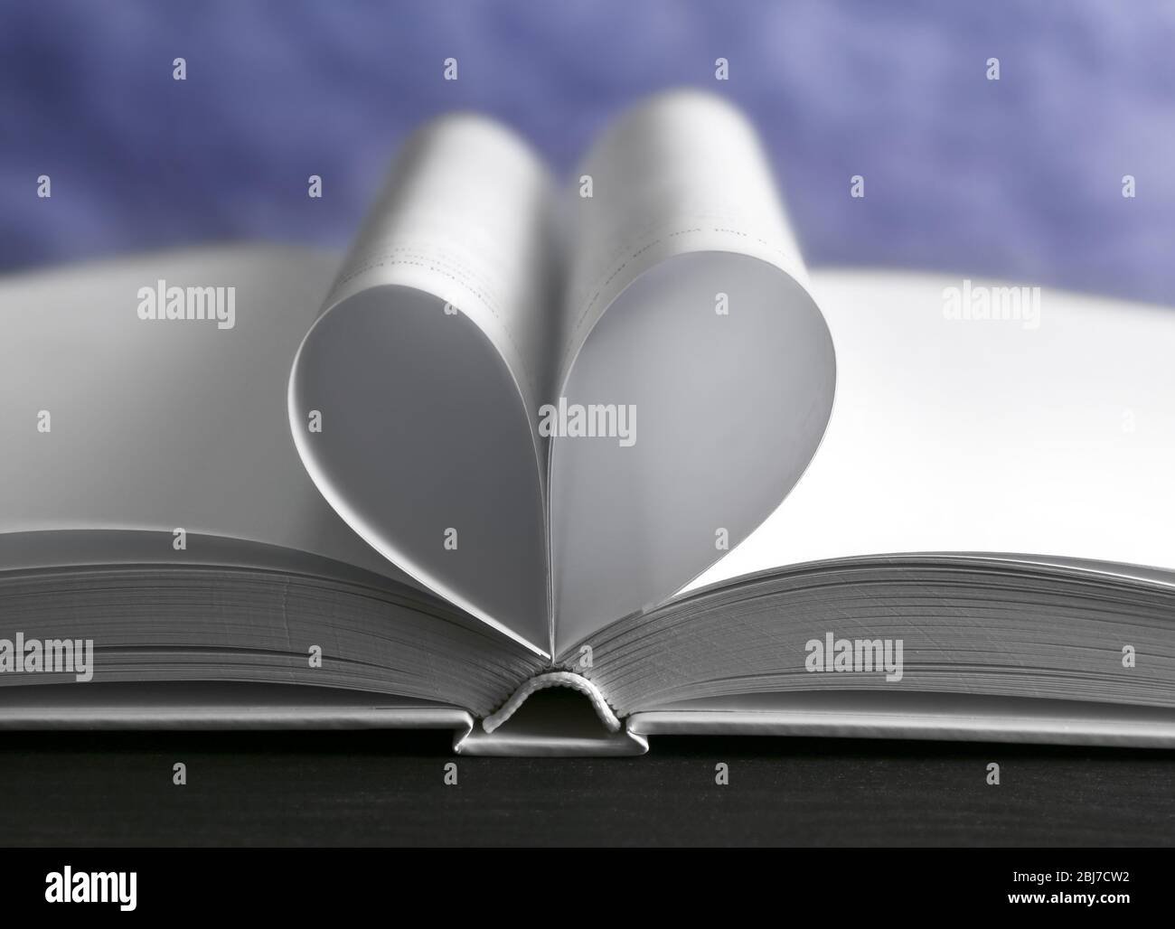Sheets of book curved into heart shape on unfocused blue background ...