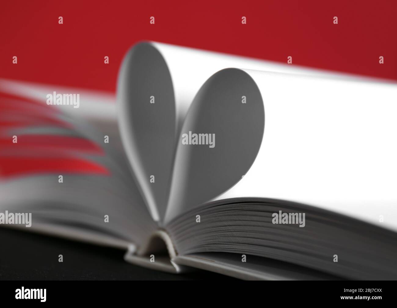 Sheets of book curved into heart shape on unfocused red background ...