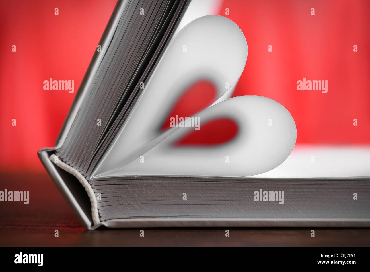 Heart from book pages on red blurred background Stock Photo - Alamy