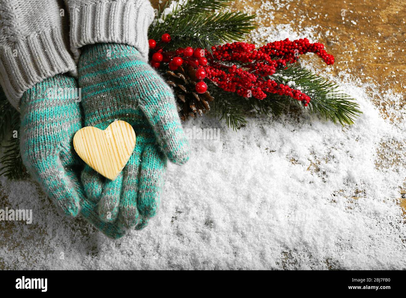 Female hands in blue mittens with decorative heart on snow background ...