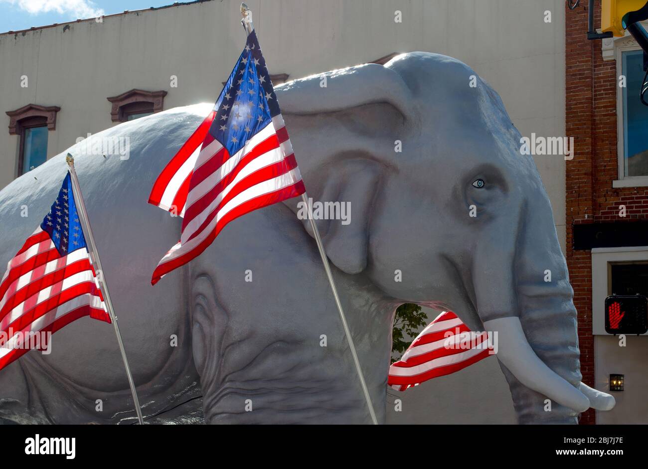 A large elephant float in a local parade is flanked by American flags ...