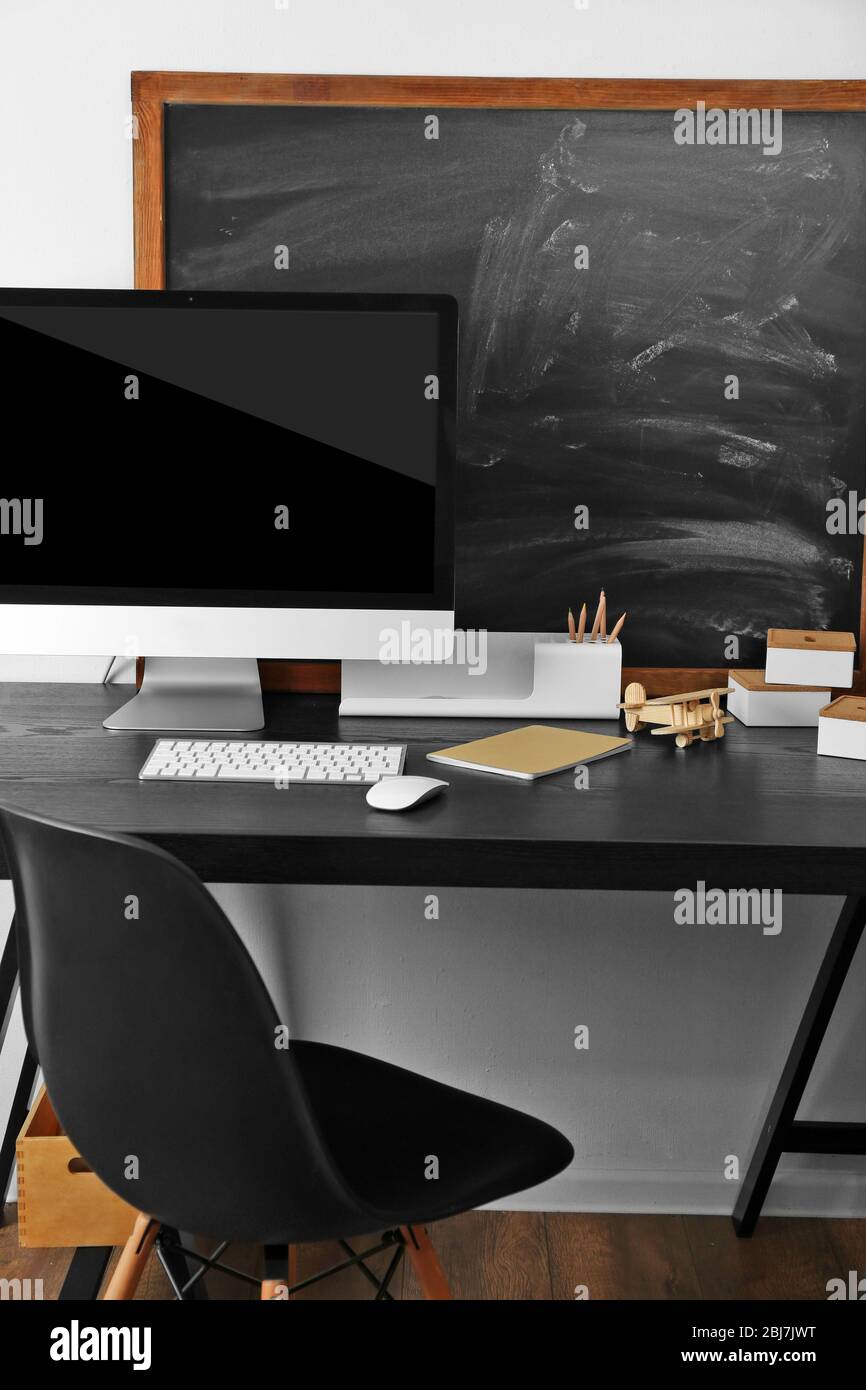 Desktop with computer monitor and other items against blackboard ...