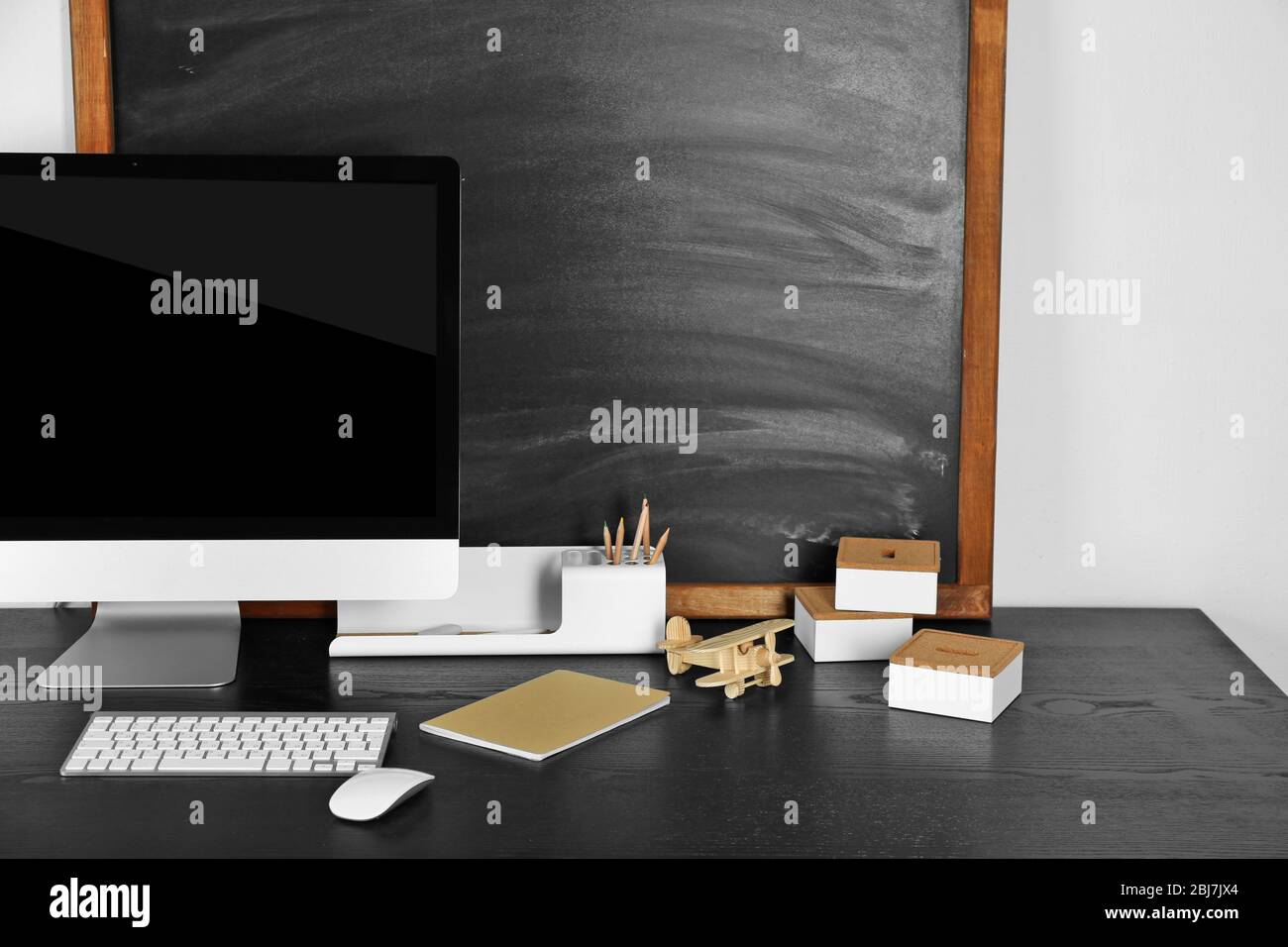 Desktop with computer monitor and other items against blackboard ...
