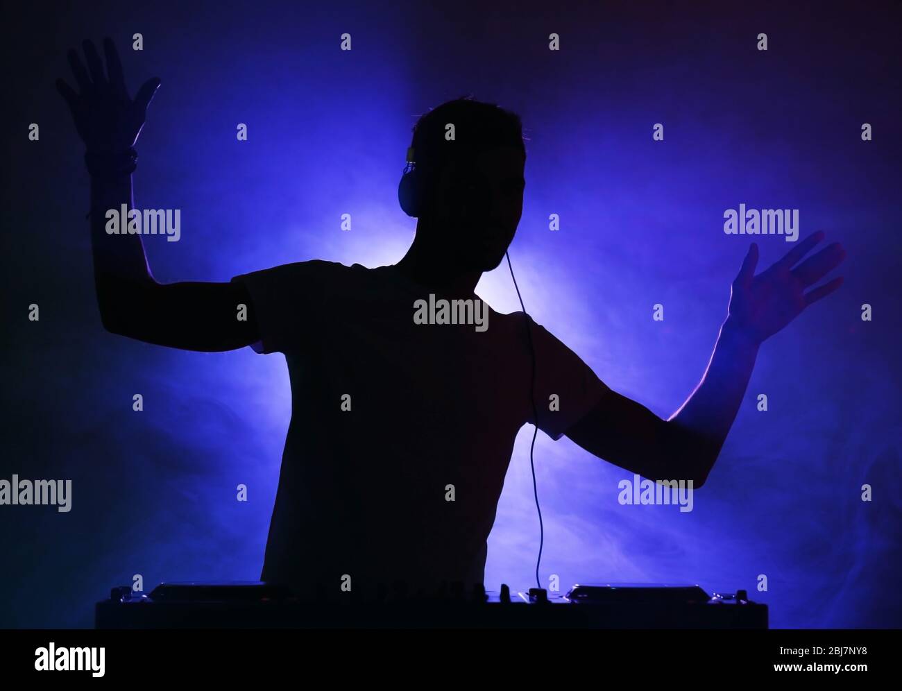 DJ playing music at mixer on color foggy background Stock Photo - Alamy