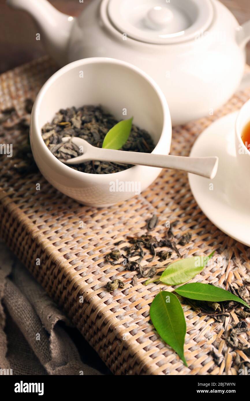 Granulated tea with green leaves in tea-set on wicker tray closeup ...